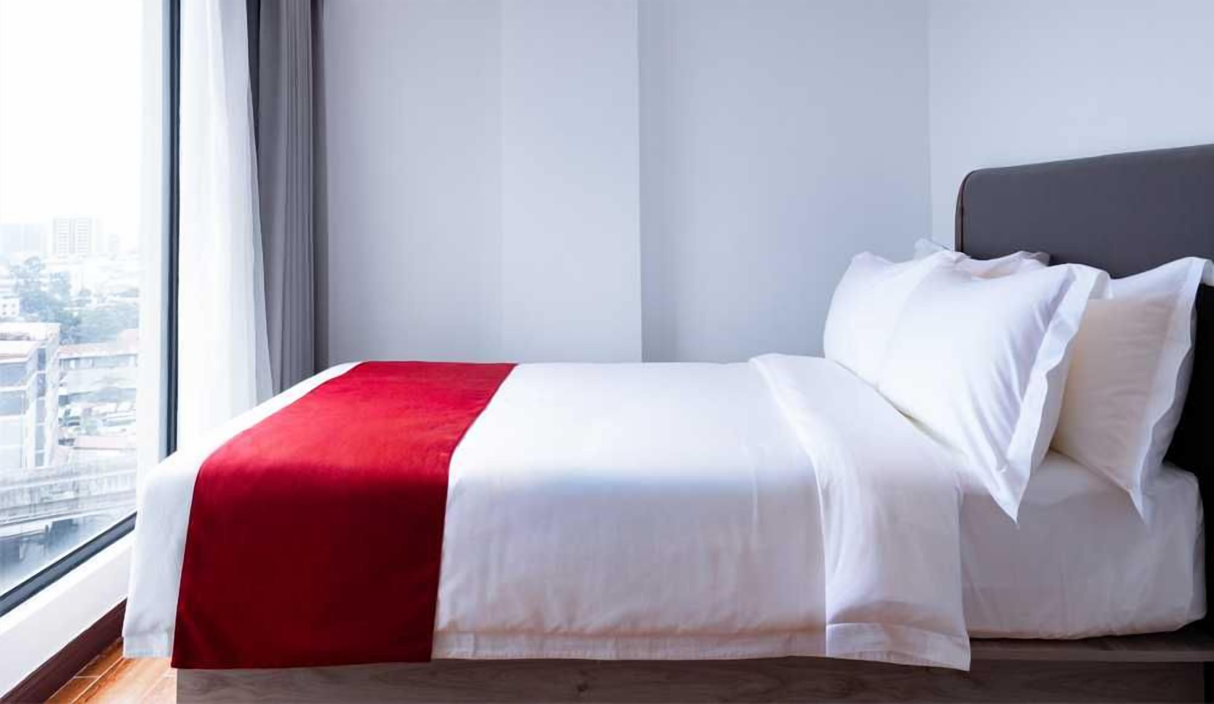 Quarto de hotel com cama, janela com cortinas e vista para prédios.