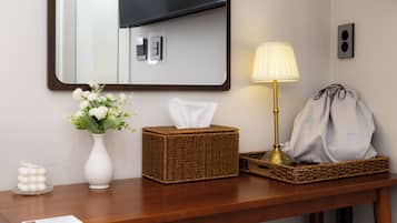 Área de recepção de um quarto de hotel com um espelho, um vaso com flores, uma caixa de lenços, um abajur e uma bolsa.