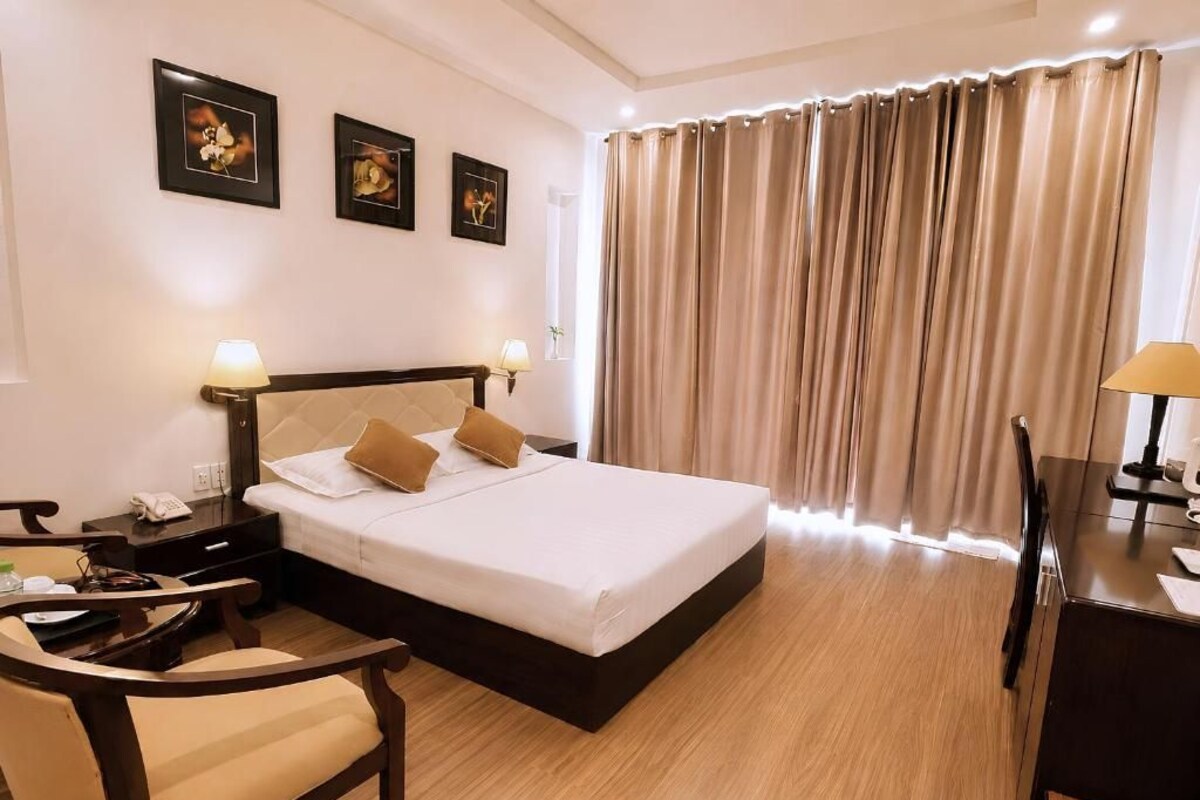 Quarto de hotel com cama, mesas de cabeceira, escrivaninha, cadeira e cortinas.