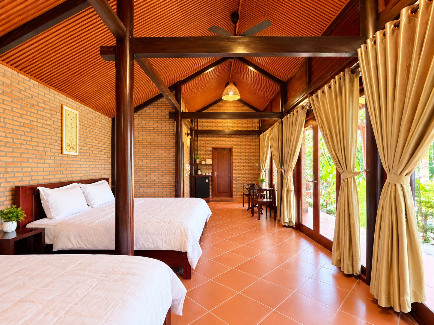 Quarto de hotel com duas camas, área de refeições e cozinha visível através de uma porta aberta.