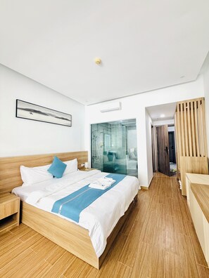 Quarto de hotel com cama grande, mesa de cabeceira, chuveiro em cabine de vidro e divisória de madeira.