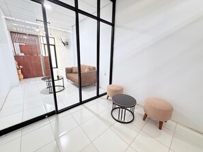 Um interior moderno com divisória de vidro, um sofá, dois pufes e uma pequena mesa redonda.