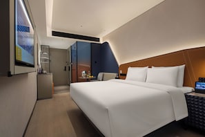 Quarto de hotel com uma cama grande, uma escrivaninha, uma cadeira e uma televisão.
