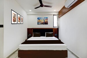 Quarto de hotel com cama, ventilador de teto, obras de arte na parede e ar condicionado.