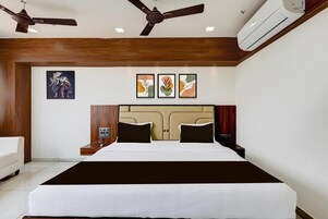 Quarto de hotel moderno com uma cama grande, ventiladores de teto, ar condicionado e obras de arte nas paredes.