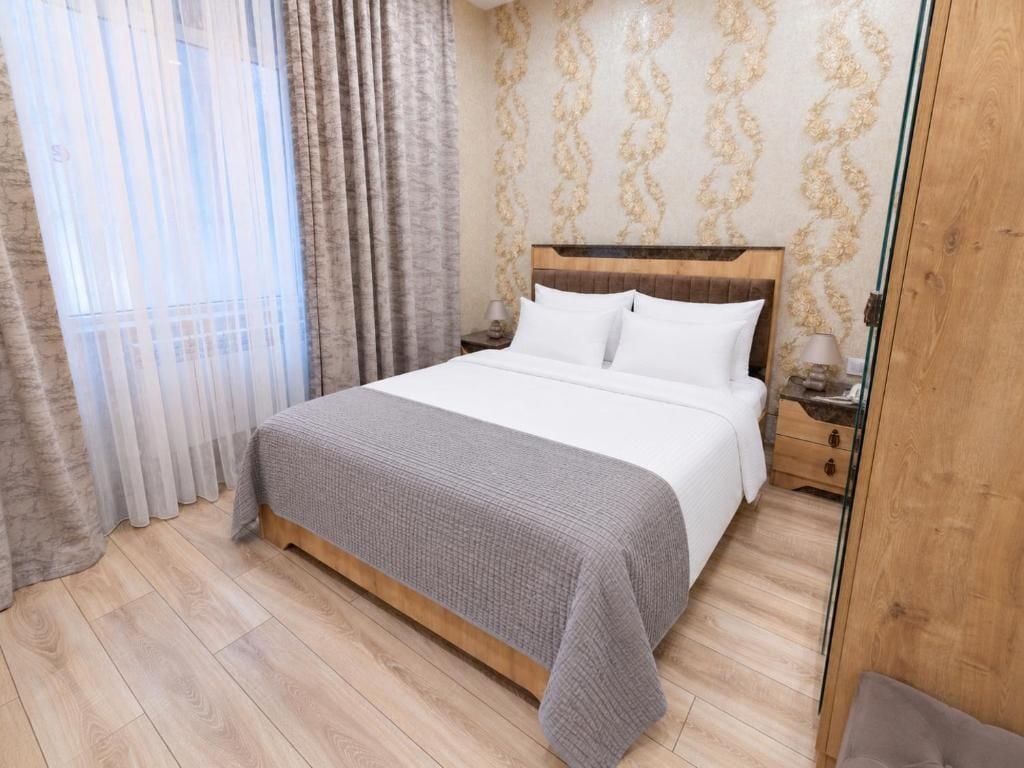 Quarto de hotel com cama, cortinas, mesa de cabeceira e guarda-roupa de madeira.