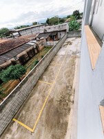 Terraço com barreira de concreto, área pavimentada com linhas amarelas e vista de edifícios com telhados vermelhos.