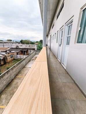 Um corredor com um banco de madeira, uma parede de concreto e vista para um edifício com janelas.