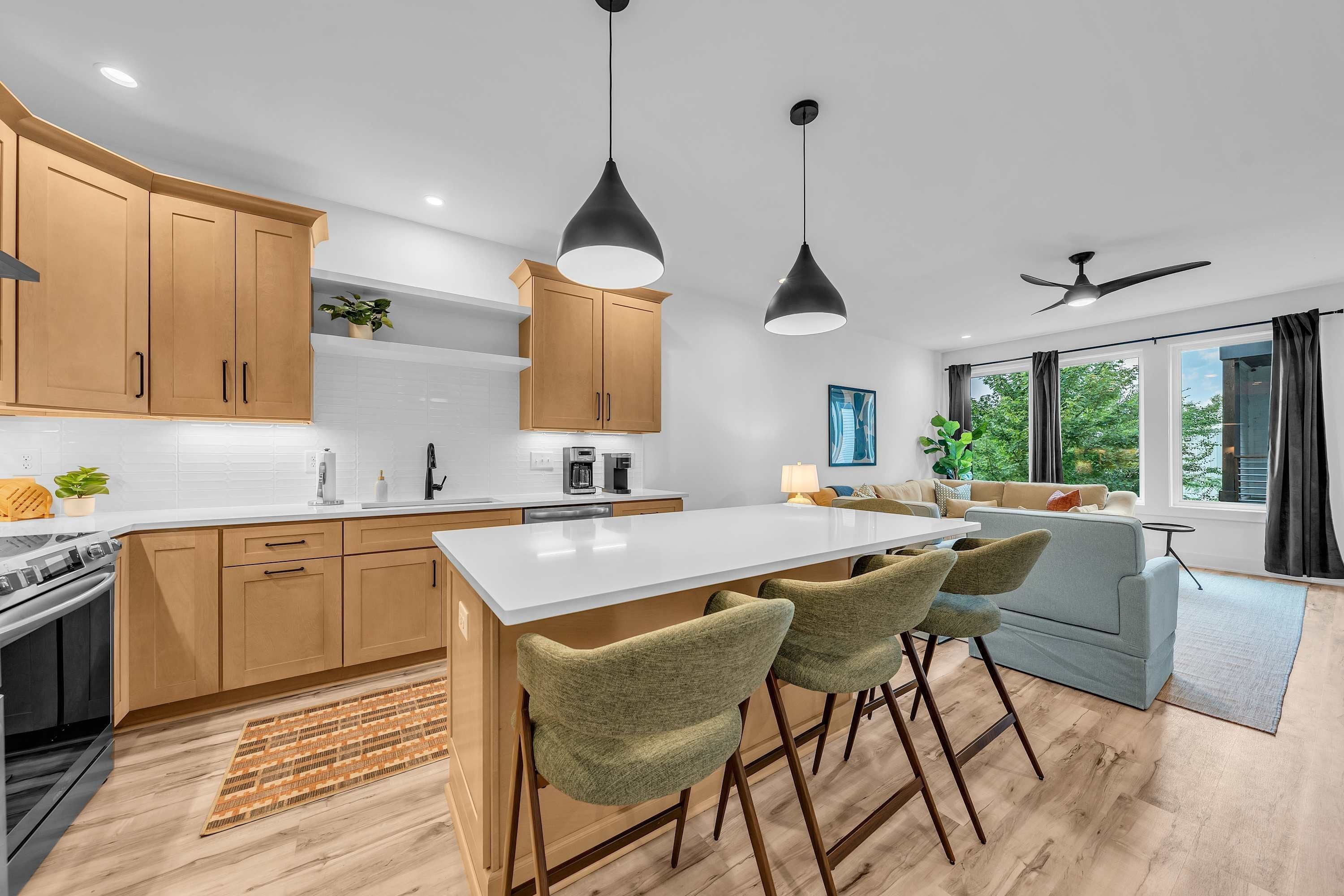 Cozinha moderna com ilha central, banquetas de bar e área de jantar com sofá.