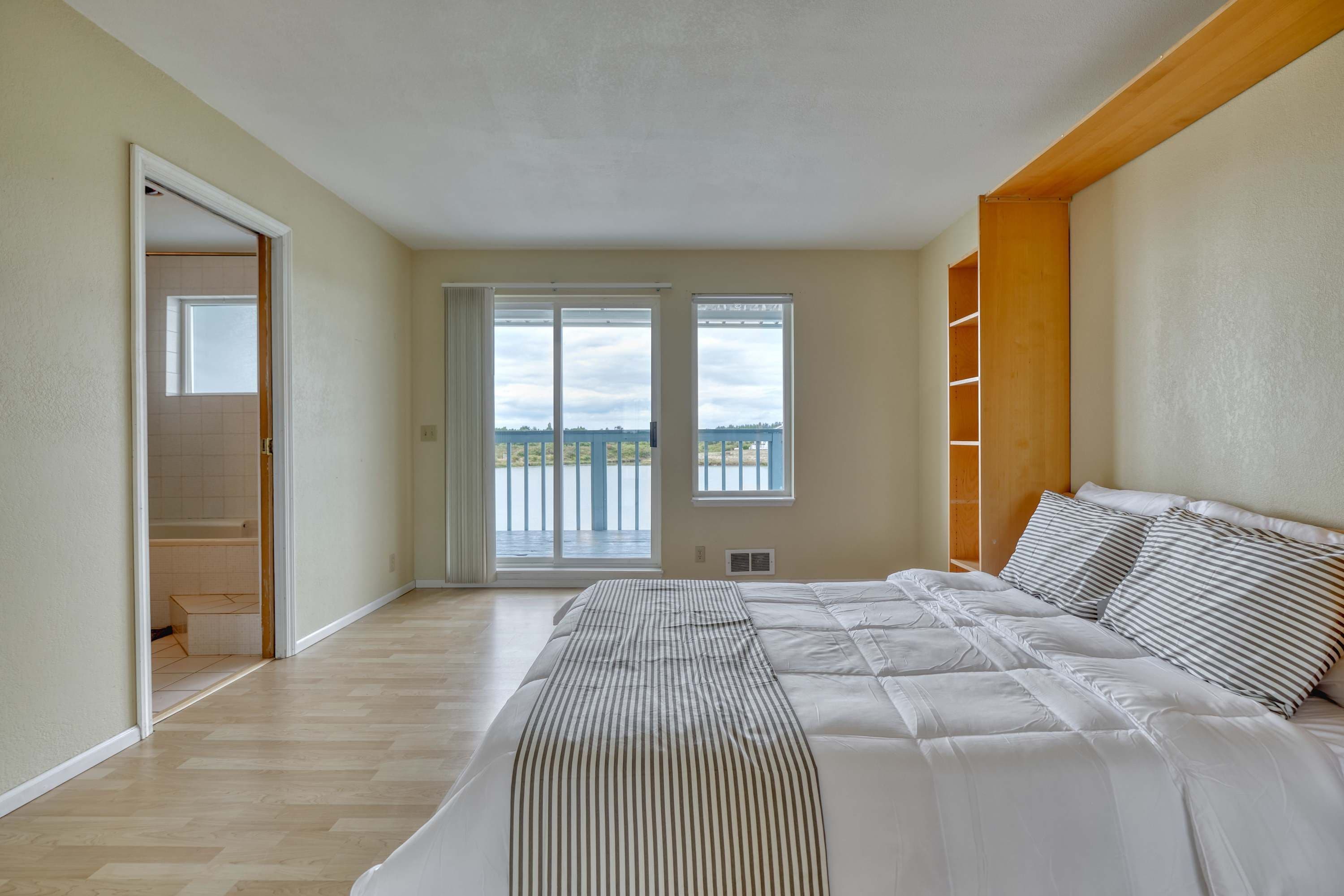 Quarto com cama grande, cabeceira de madeira, vista para o exterior e porta de vidro deslizante.