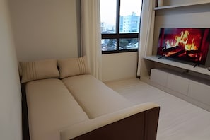 Quarto moderno com cama, televisão em móvel e janela com vista para edifícios.