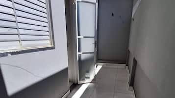 Um corredor estreito com piso de azulejos, uma porta que dá para um quarto e uma janela com persianas.