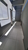 Um corredor estreito com piso de azulejos, uma porta que dá para um quarto e uma janela com persianas.