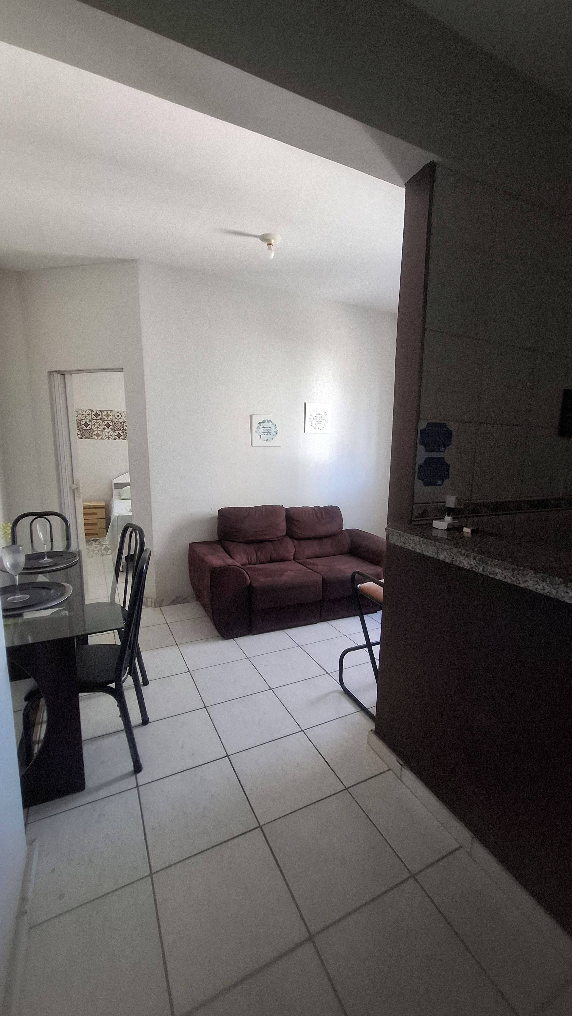 Sala de estar com sofá, mesa de jantar com cadeiras e área de cozinha com bancada.
