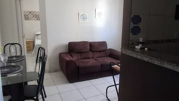 Sala de estar com sofá, mesa de jantar com cadeiras e área de cozinha com bancada.