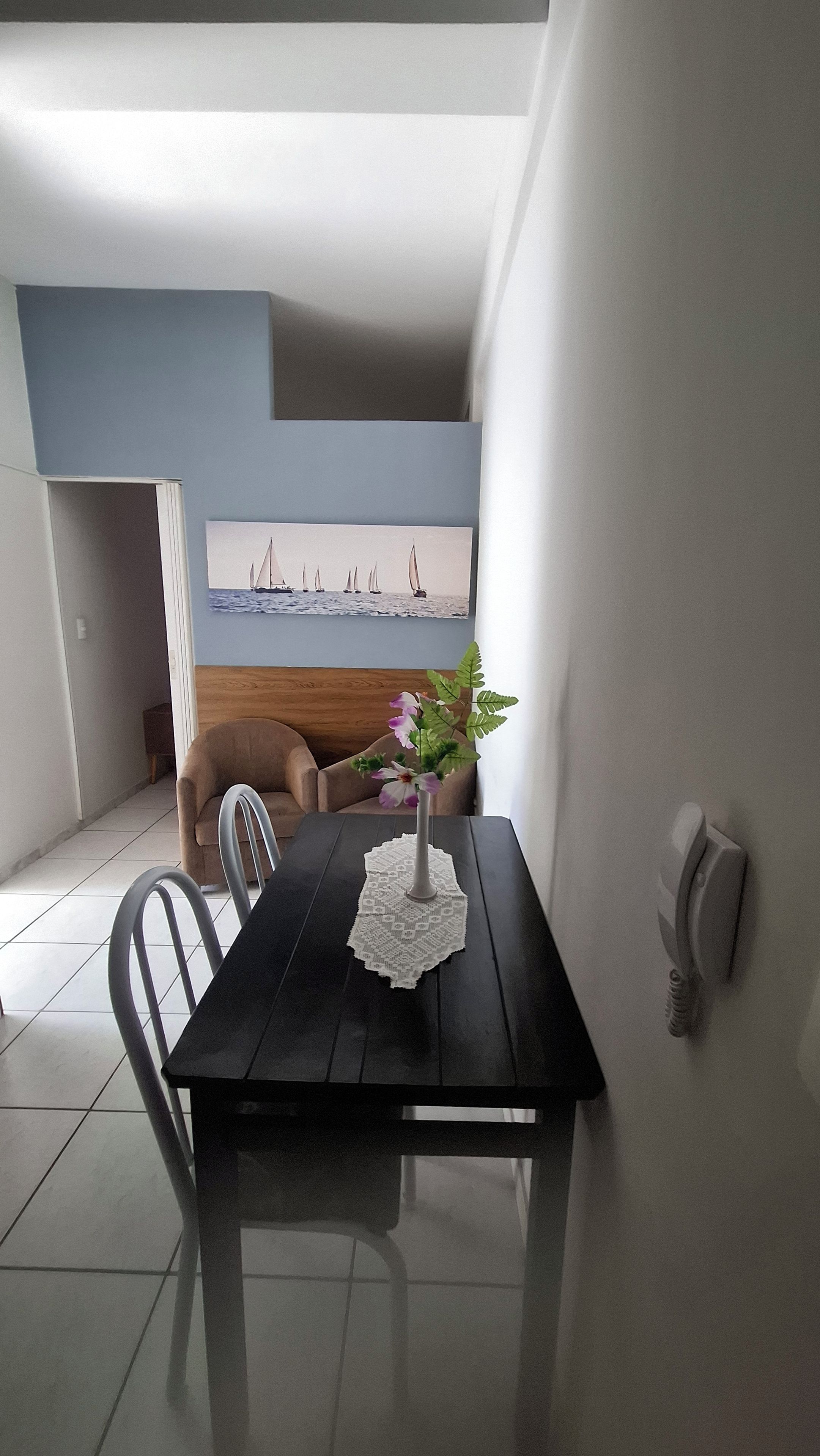 Uma sala de jantar com uma mesa, cadeiras, um vaso de flores e um quadro na parede.