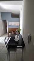 Uma sala de jantar com uma mesa, cadeiras, um vaso de flores e um quadro na parede.