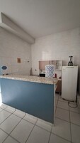 Uma cozinha com bancada azul, armários brancos, geladeira branca e máquina de café.