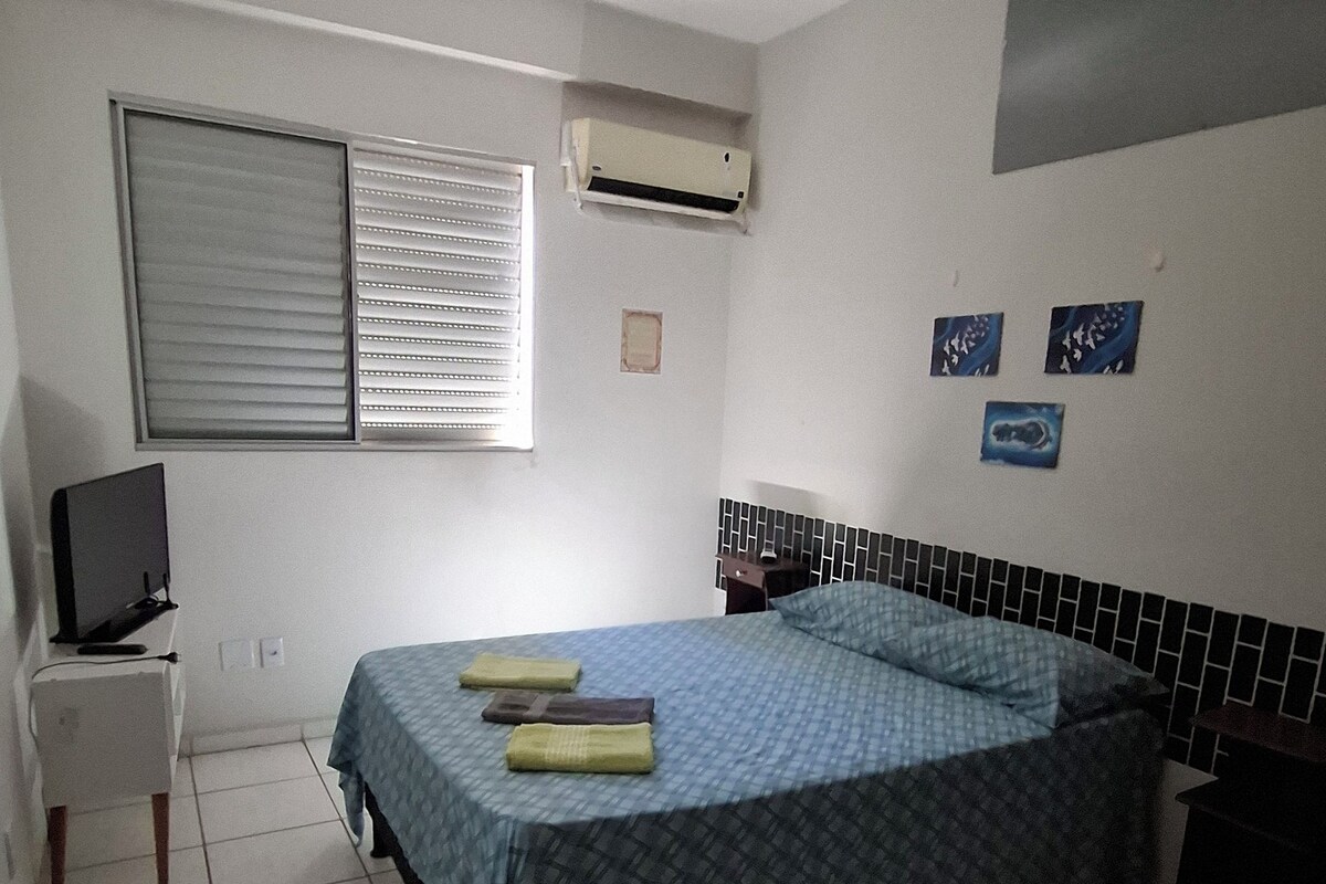 Quarto com cama, televisão, mesa de cabeceira e ar condicionado.
