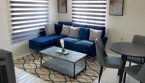 Uma sala de estar com um sofá azul, uma mesa de centro e uma mesa de jantar com cadeiras.