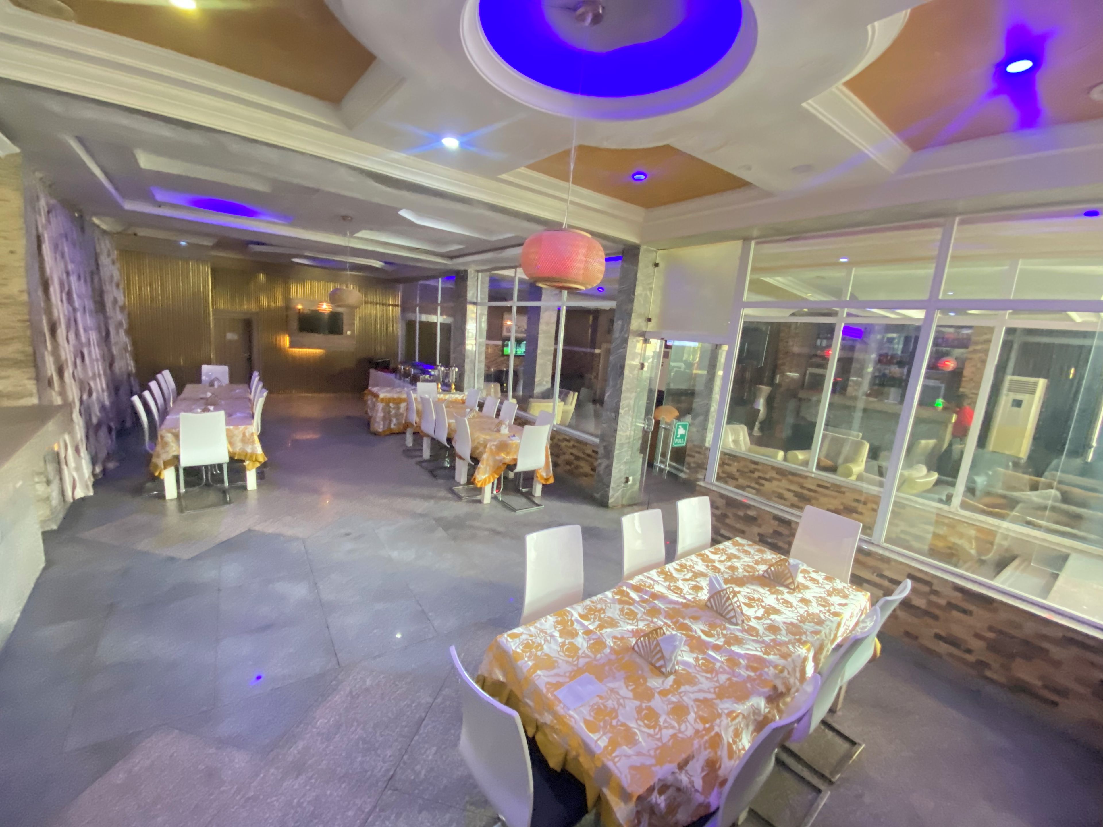 Um restaurante com várias mesas e cadeiras, um design de teto moderno e janelas amplas.