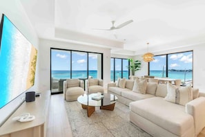 Uma sala de estar moderna com uma televisão grande, assentos confortáveis e vista para o oceano.