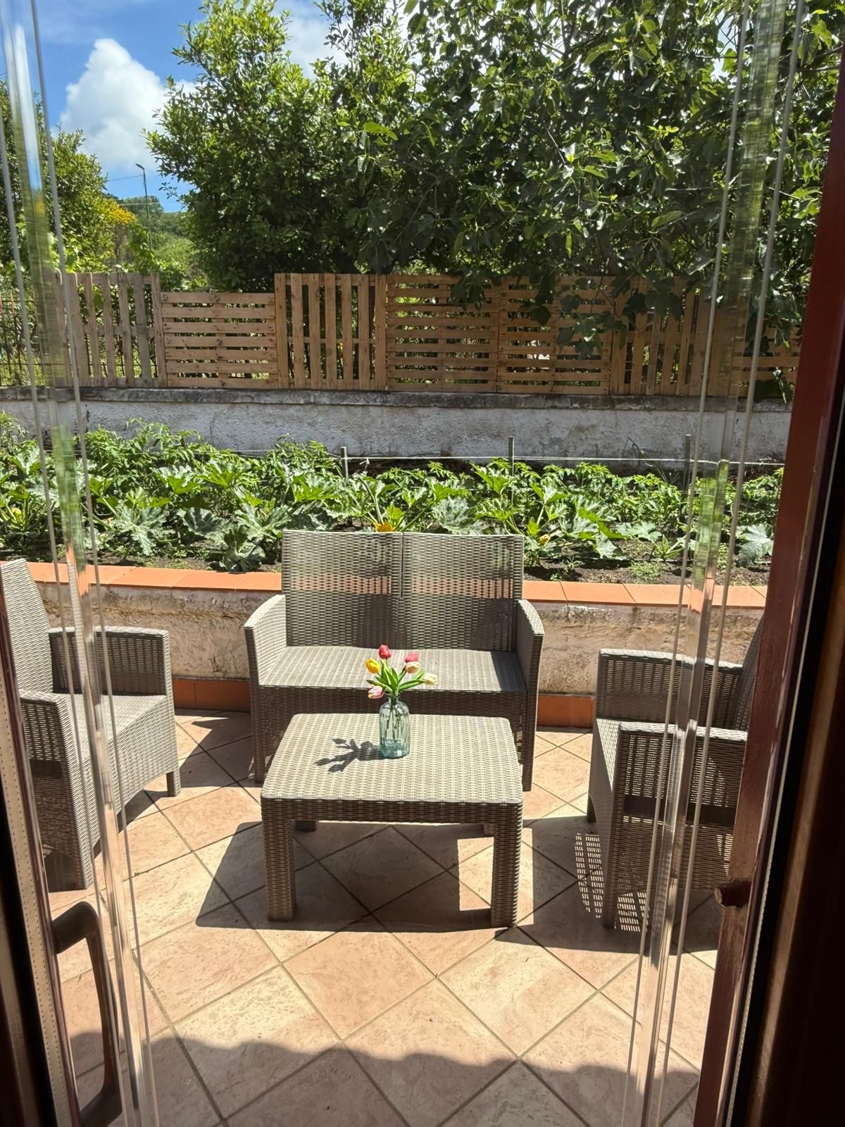 Pátio externo com móveis de vime e uma pequena mesa com um vaso de flores.
