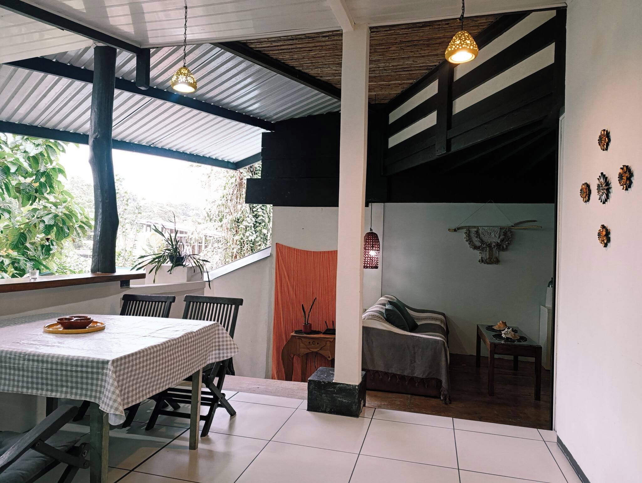 Uma sala de jantar com uma mesa posta para dois, um sofá e uma pequena mesa com uma planta.