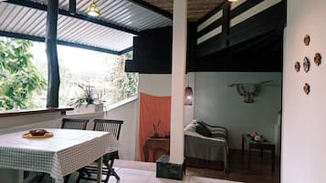 Uma sala de jantar com uma mesa posta para dois, um sofá e uma pequena mesa com uma planta.