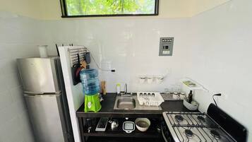 Cozinha compacta com geladeira, pia, fogão e janela com vista para área verde.