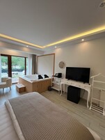 Quarto de hotel moderno com uma cama grande, uma escrivaninha com TV de tela plana, área de estar com banheira de hidromassagem e vista para o exterior.