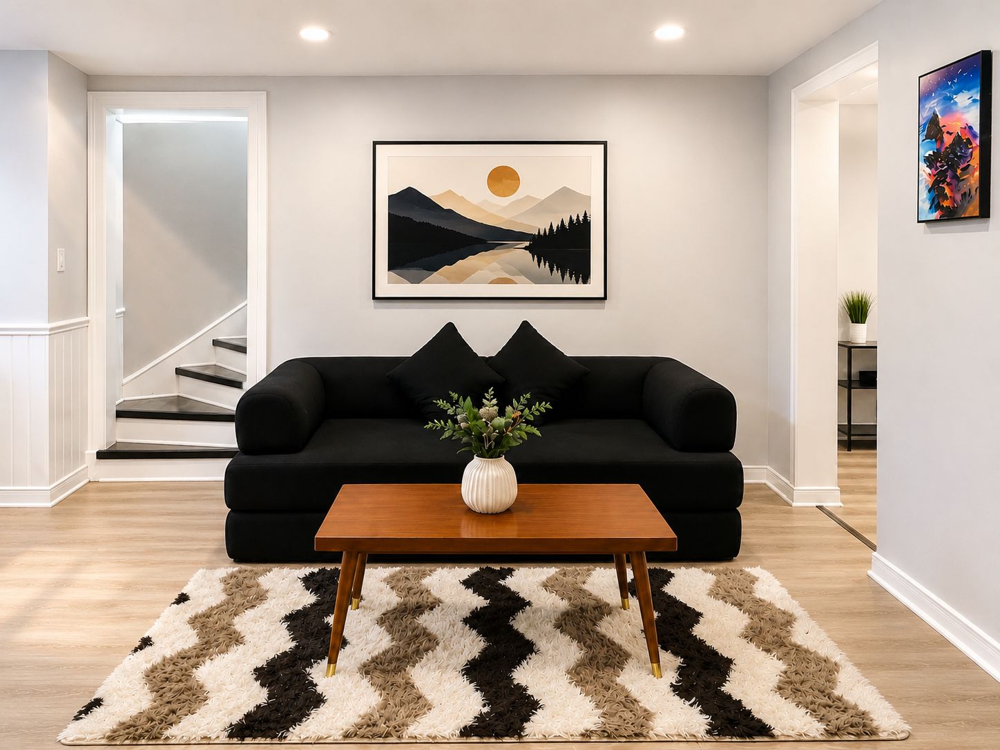 Sala de estar com sofá preto, mesa de centro de madeira e quadro com paisagem na parede.
