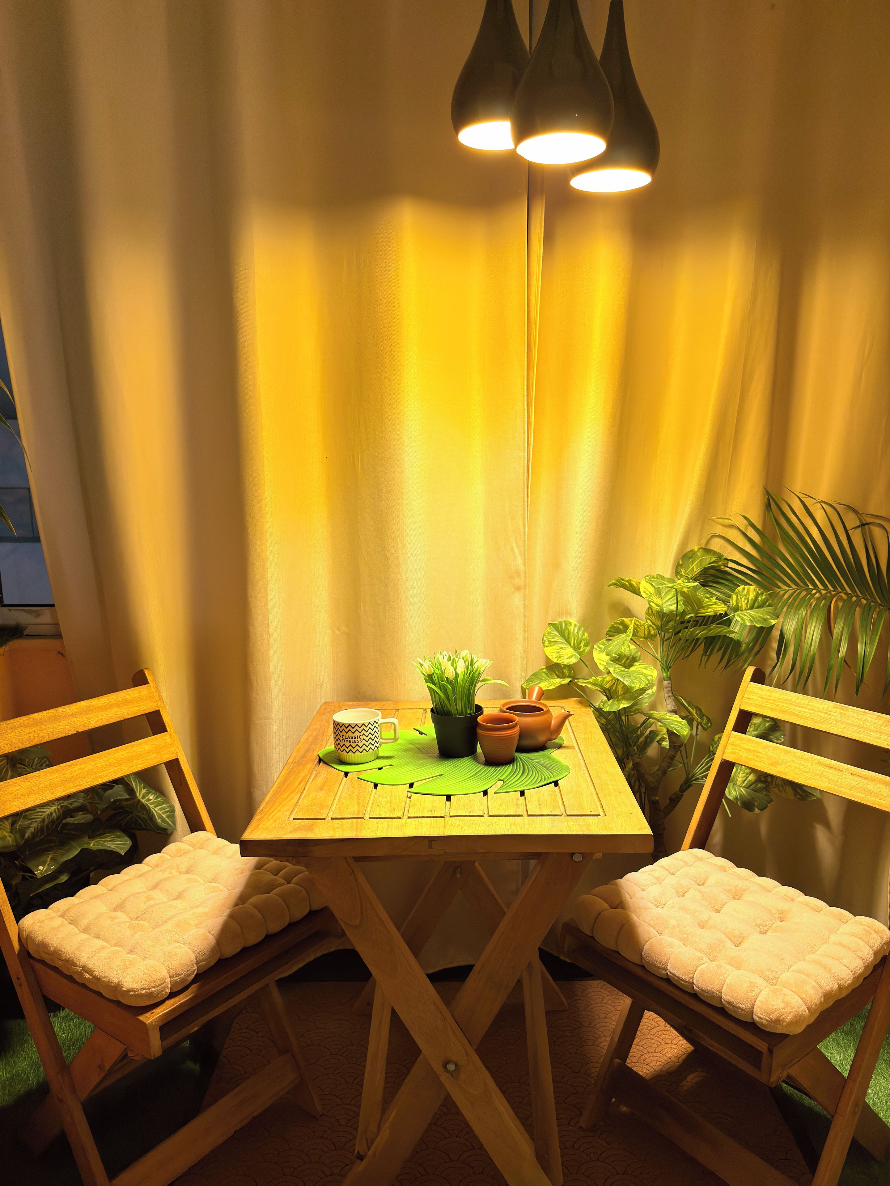 Uma pequena mesa com duas cadeiras, um vaso de planta e uma chaleira.