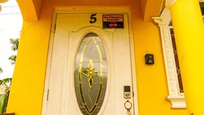 Um edifício com fachada amarela, o número '5' acima da porta e um aviso de 'Não Fumar'.