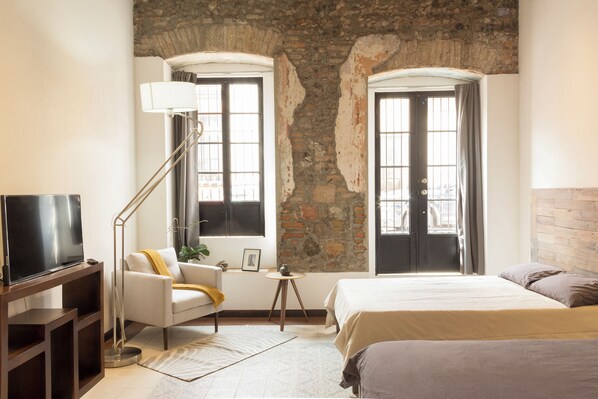 Quarto com televisão, cadeira, cama, mesa pequena e abajur.