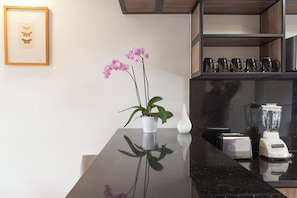 Uma bancada de cozinha com um liquidificador, uma torradeira e uma orquídea em vaso.