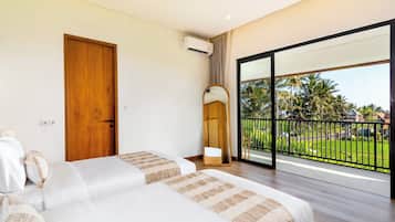 Quarto de hotel com uma grande porta de vidro deslizante que dá para uma varanda com vista para palmeiras e um gramado verde.