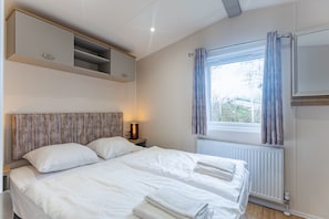 Quarto com cama, mesa de cabeceira com luminária, janela com cortinas e prateleiras embutidas sobre a cama.