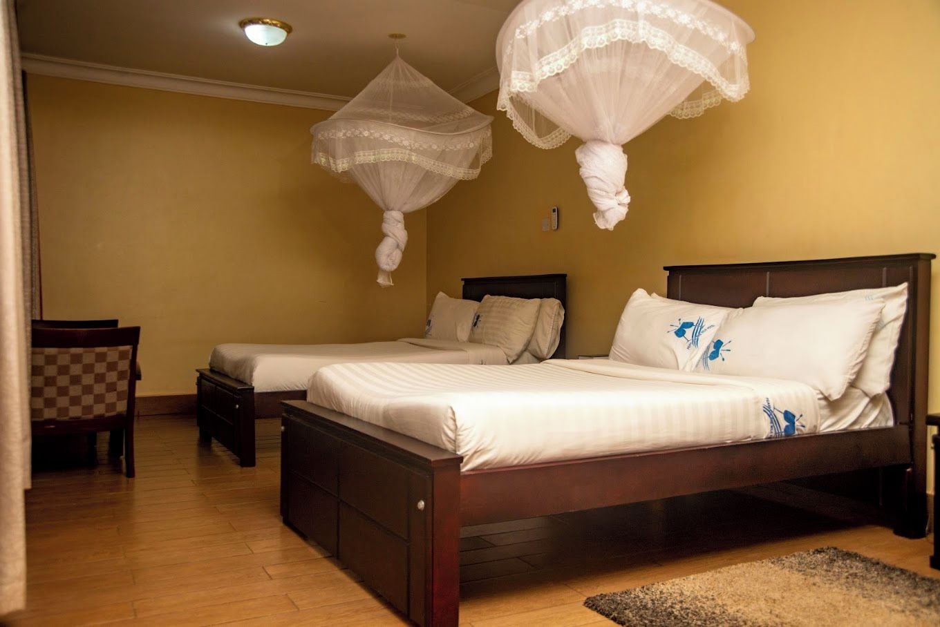 Quarto de hotel com duas camas, uma cadeira e uma mesinha de cabeceira.