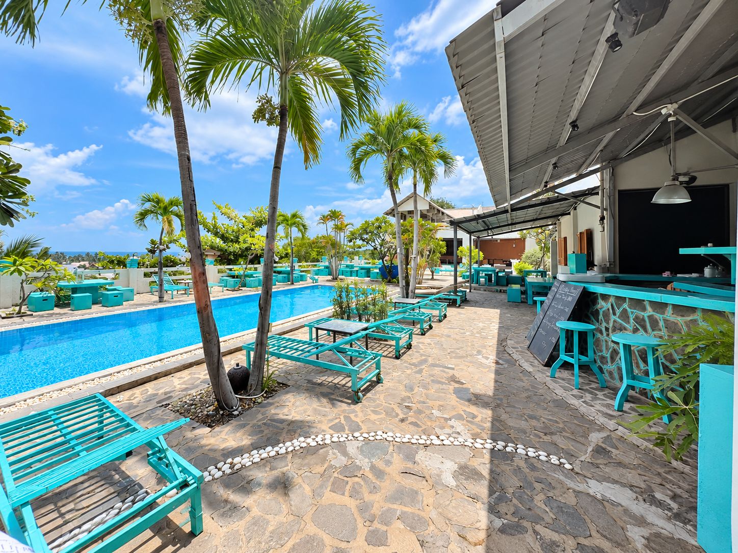 Área da piscina com um terraço de pedra, espreguiçadeiras turquesa e um bar com parede de pedra.