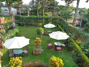 Um jardim bem cuidado com áreas de estar, incluindo mesas e cadeiras, cercado por vegetação exuberante e árvores.