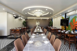 Uma sala de conferência com uma longa mesa posta para uma reunião, cercada por cadeiras, com um candelabro e unidades de ar condicionado nas paredes.