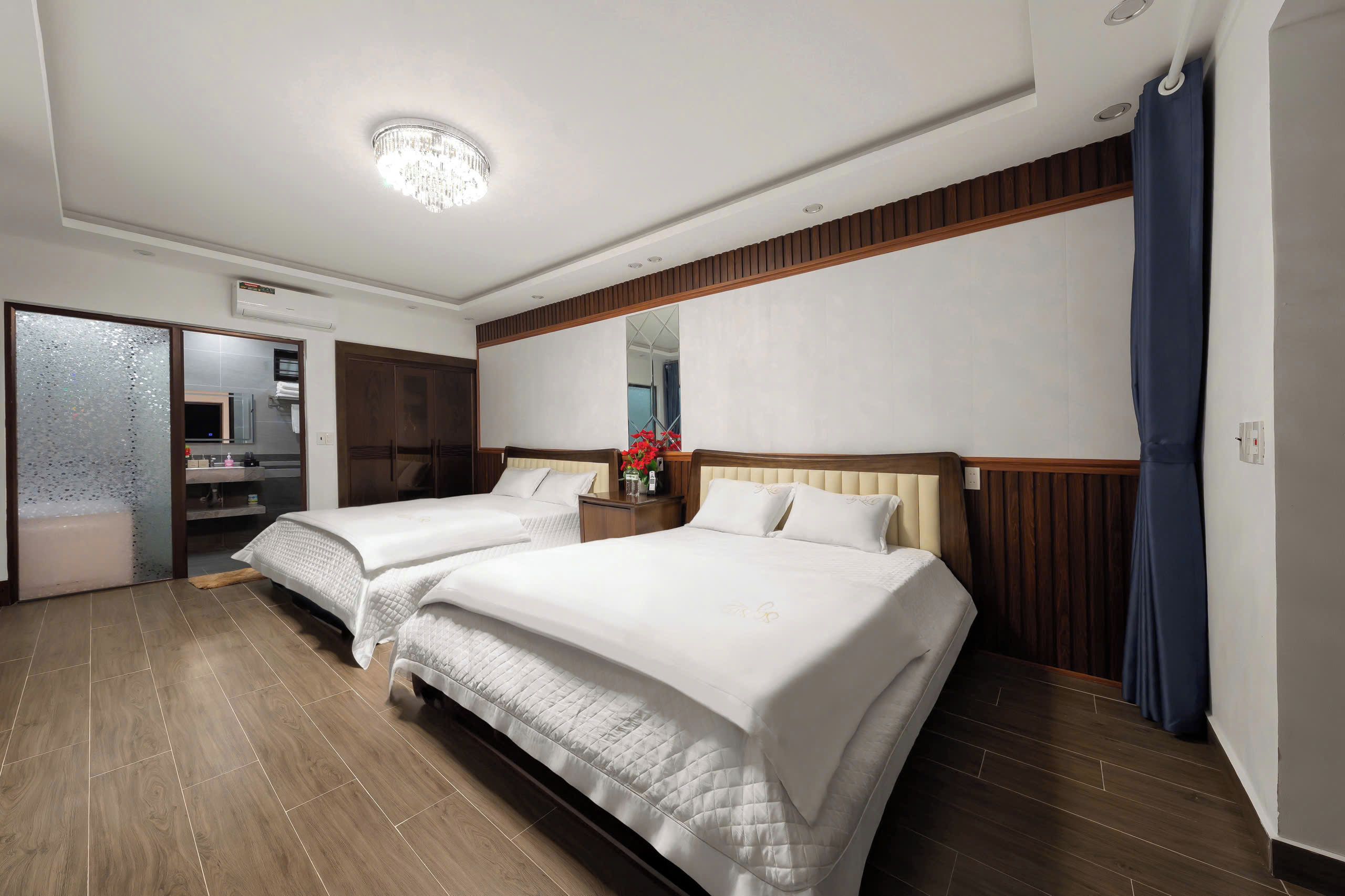 Quarto de hotel com duas camas, piso de madeira, luminária no teto e espelho na parede.