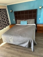 Quarto com uma cama grande, cabeceira com padrão quadriculado, duas mesas de cabeceira e luminária de parede.