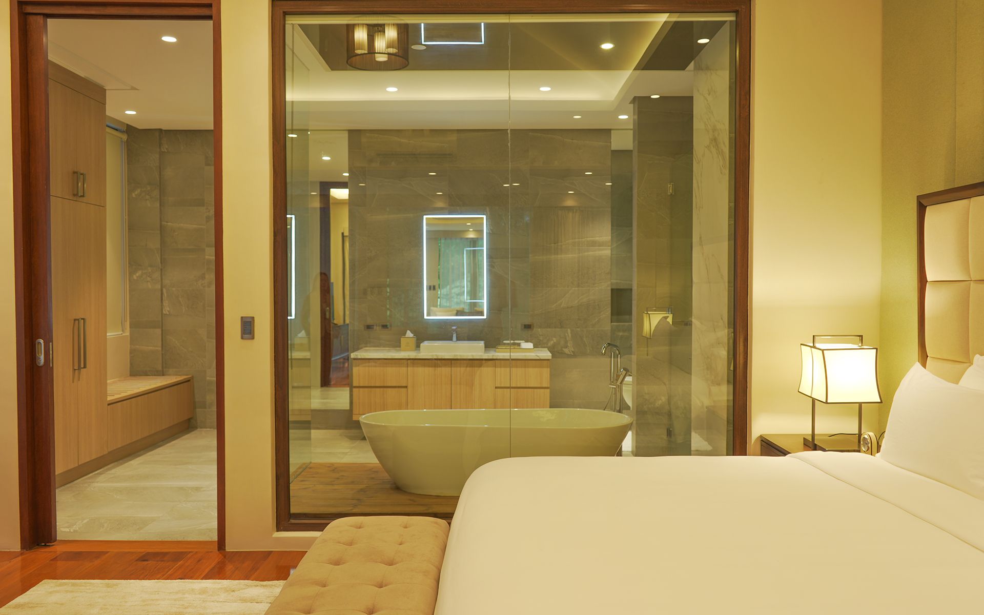 Quarto de hotel moderno com uma cama grande, banheiro com paredes de vidro com banheira e área de chuveiro separada.