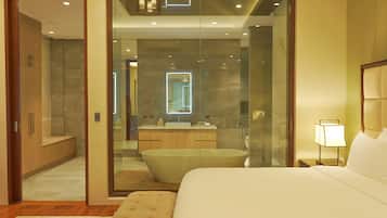 Quarto de hotel moderno com uma cama grande, banheiro com paredes de vidro com banheira e área de chuveiro separada.