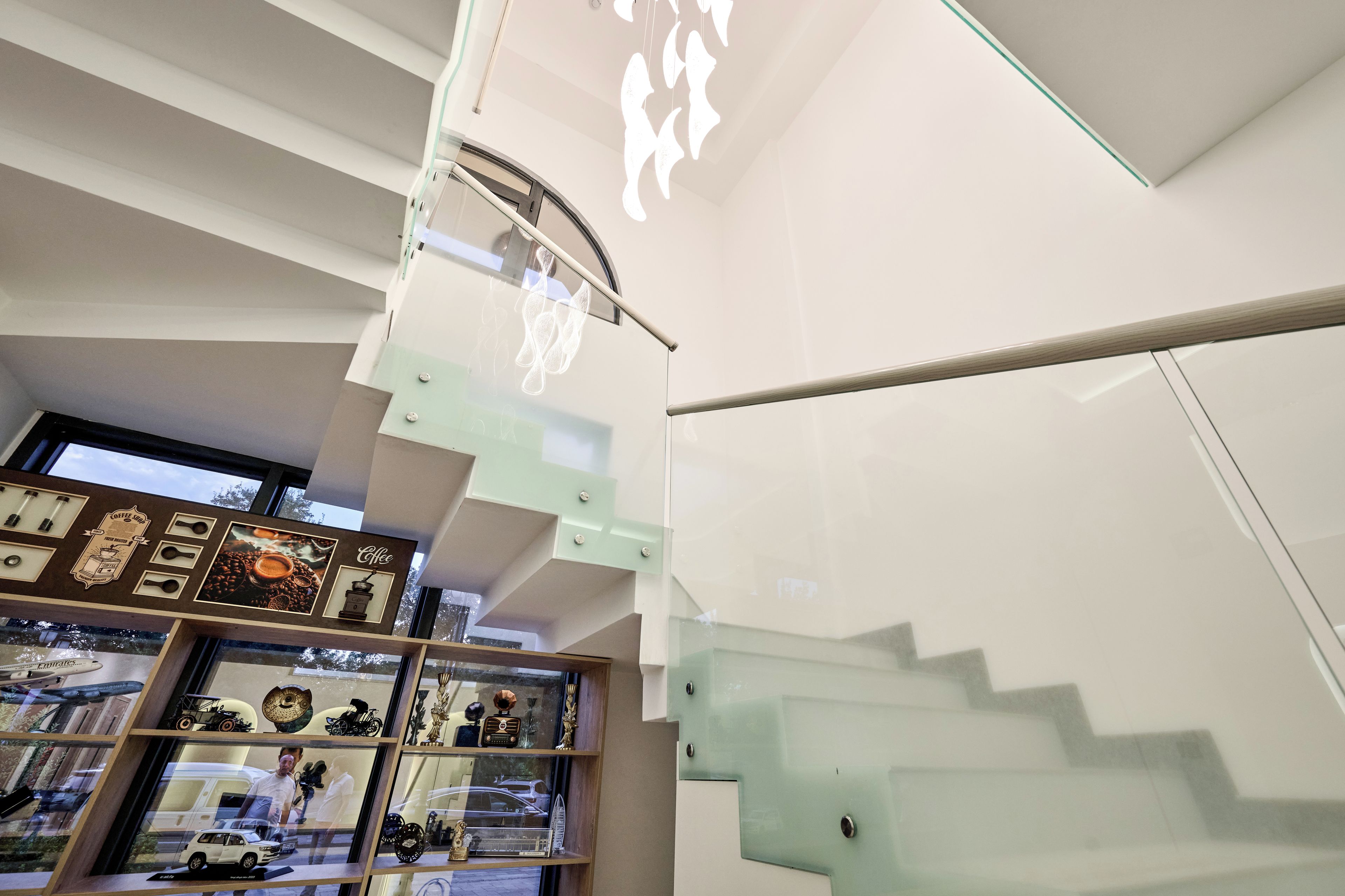 Interior moderno com escada, guarda-corpos de vidro e diversos objetos expostos, incluindo itens de coleção sobre café.