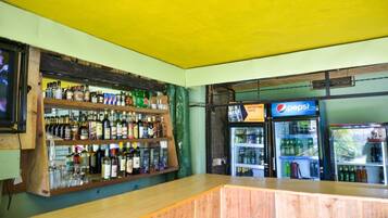Zona de bar com prateleiras cheias de garrafas de bebidas, um refrigerador de Pepsi e um balcão de madeira.