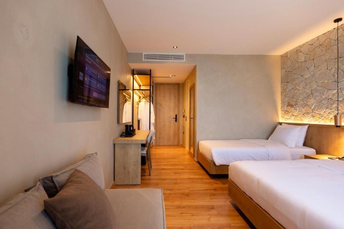 Quarto de hotel com cama, escrivaninha, cadeira, televisão e guarda-roupa.