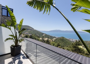 Uma varanda com vista para a paisagem costeira, incluindo colinas e um corpo de água.